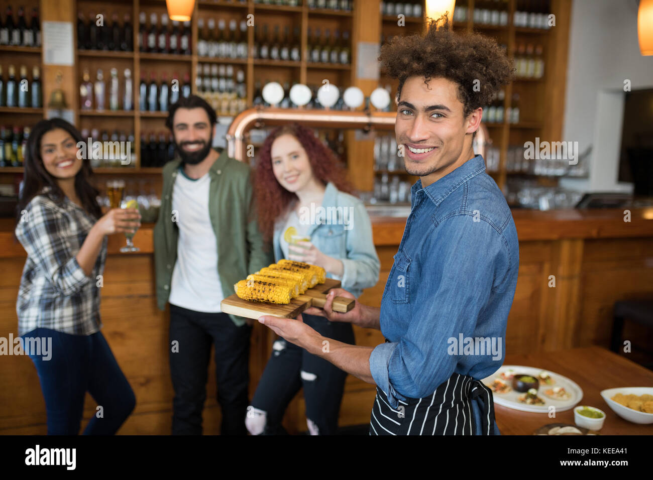 Portrait of smiling waiter serving tray of baby corn to customers in ...