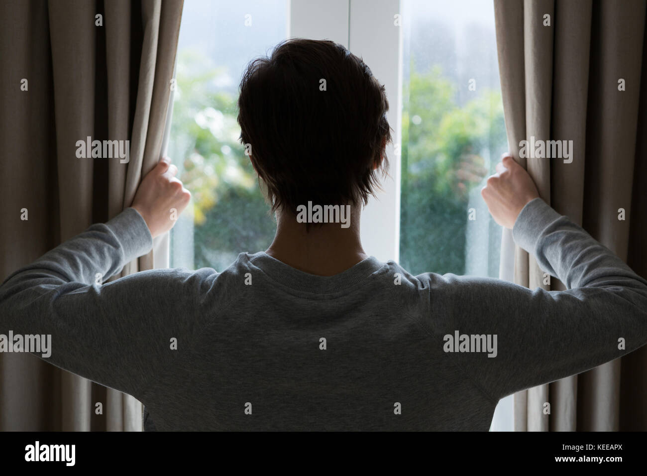 Rear view of woman looking through window at home Stock Photo - Alamy