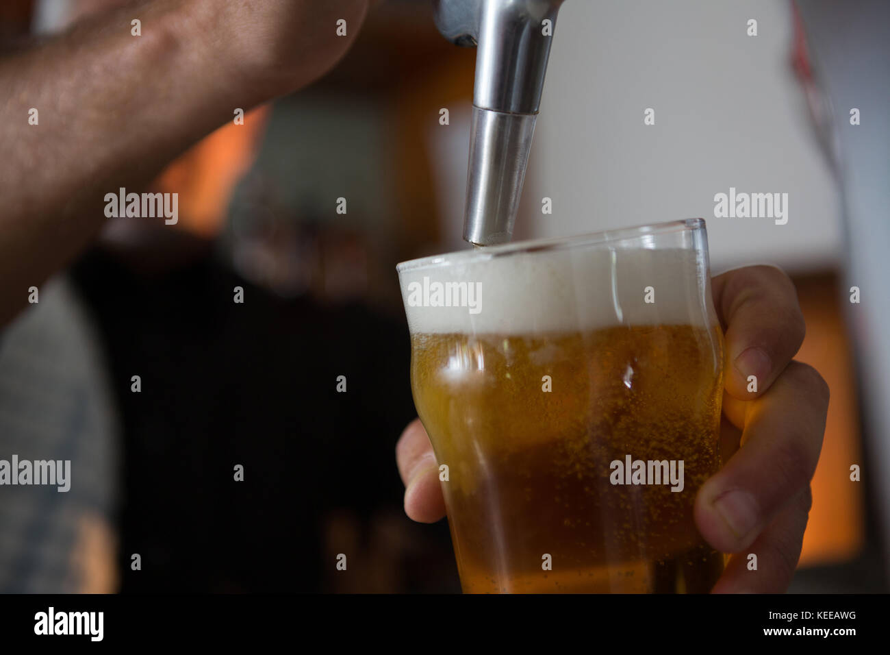 Mid-section of brewer filling beer in beer glass from beer pump in bar ...