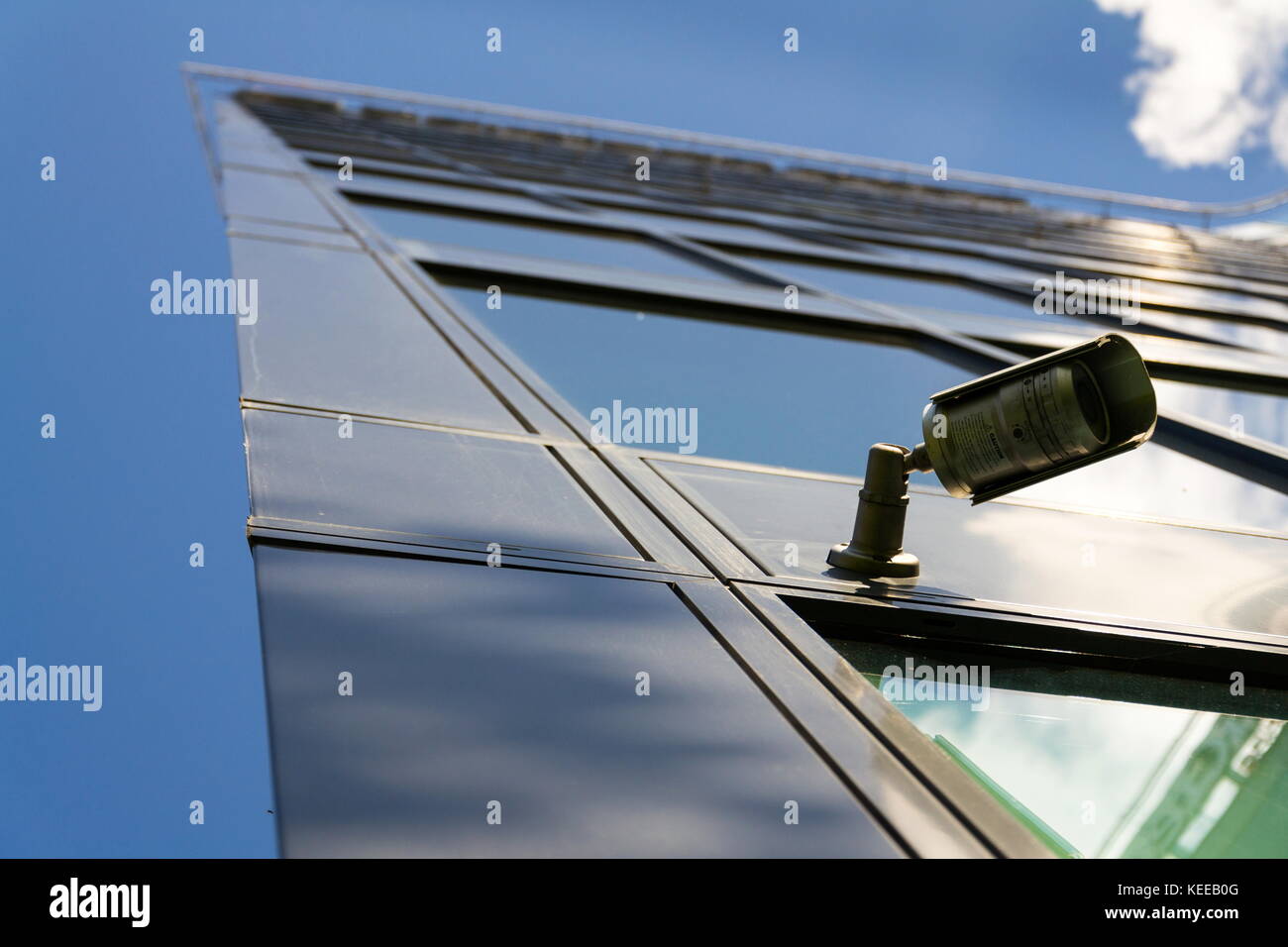 Modern security camera attached to wall with windows in background ...