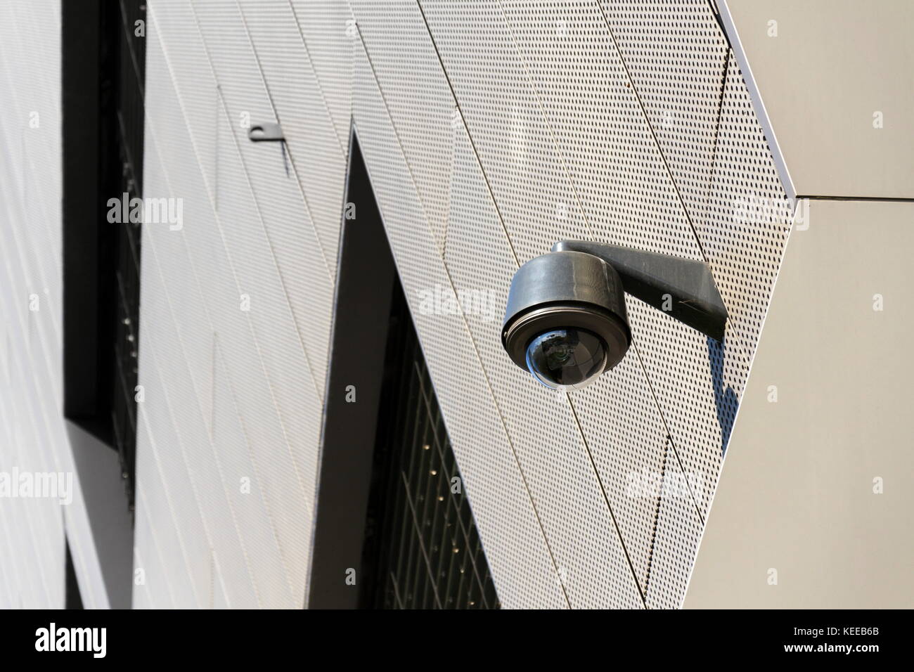 Modern security camera attached to wall with windows in background ...