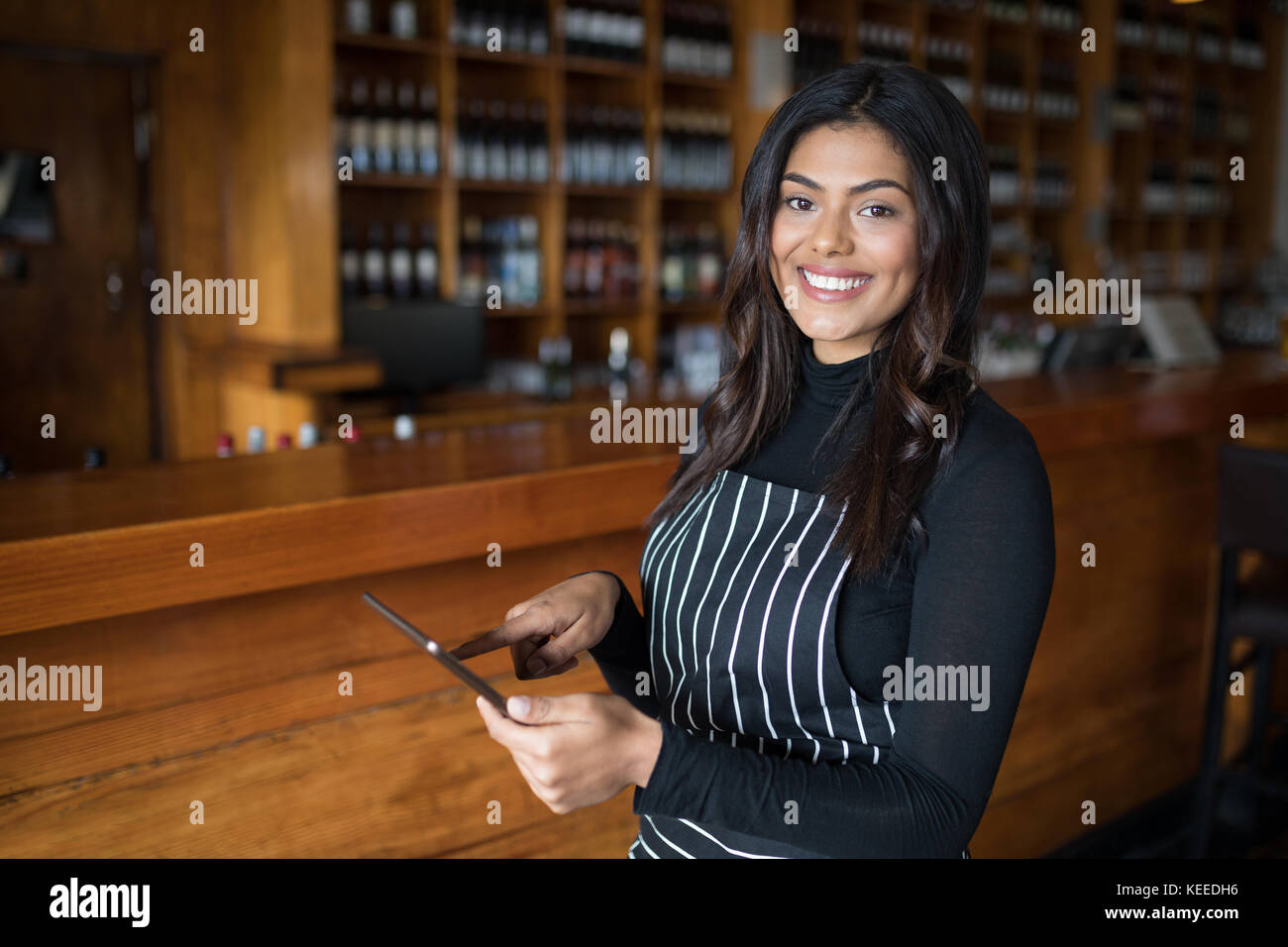 Portrait of smiling waitress using digital tablet at counter in bar ...