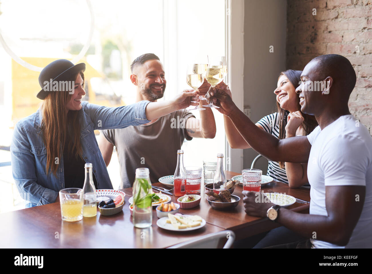 Group of four young people laughing and sitting at table in restaurant ...