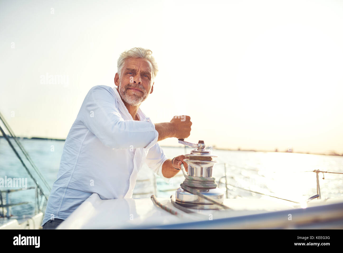 Mature man standing on the deck of a boat using a rope winch while out ...