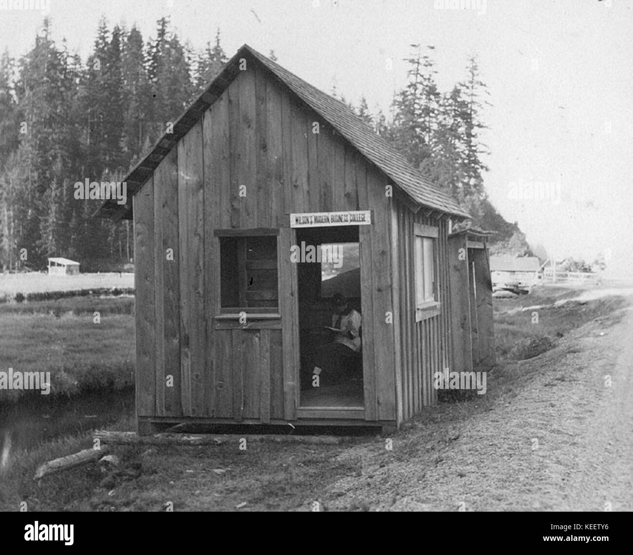 Woman seated inside shack with sign Wilson's Modern Business College ...