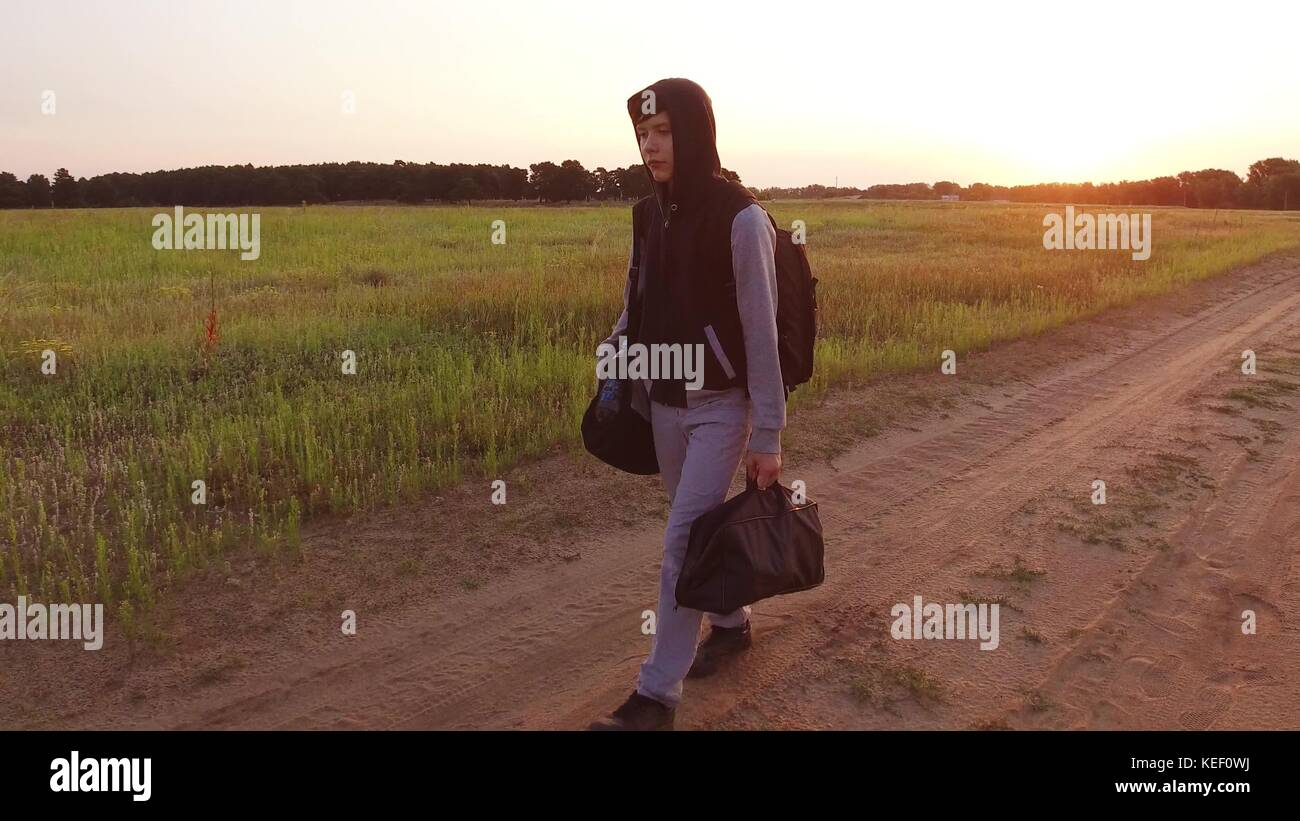 Boy teen traveling. Boy teenage tramp walking along the road in hood ...