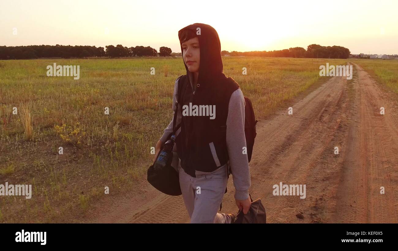 Boy teen traveling. Boy teenage tramp walking along the road in a hood ...