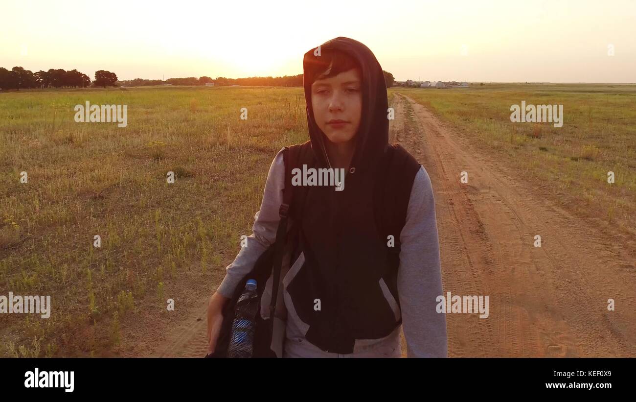 Boy teen traveling. Boy teenage tramp walking along the road in a hood ...