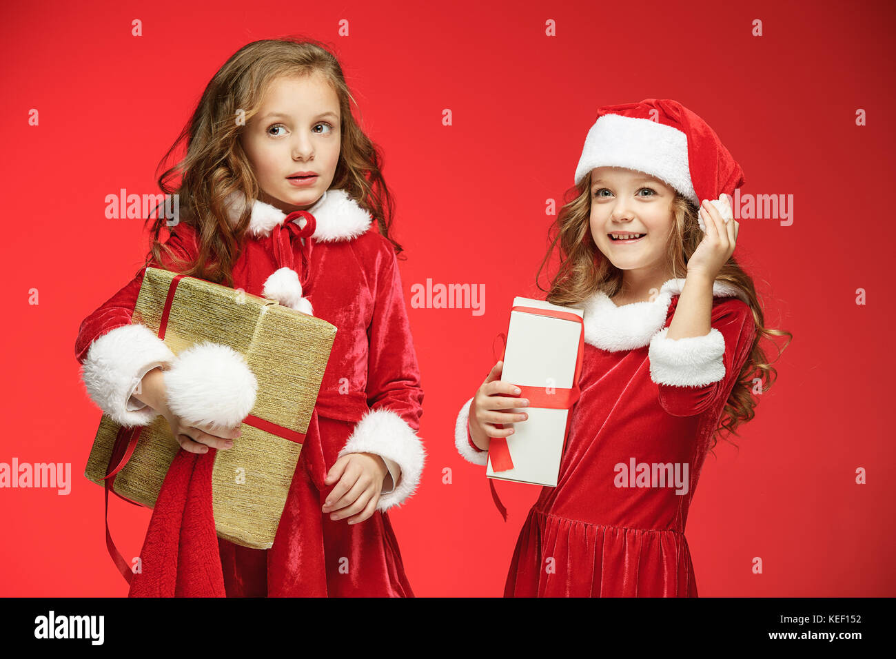 Two happy girls in santa claus hats with gift boxes at red studio Stock ...