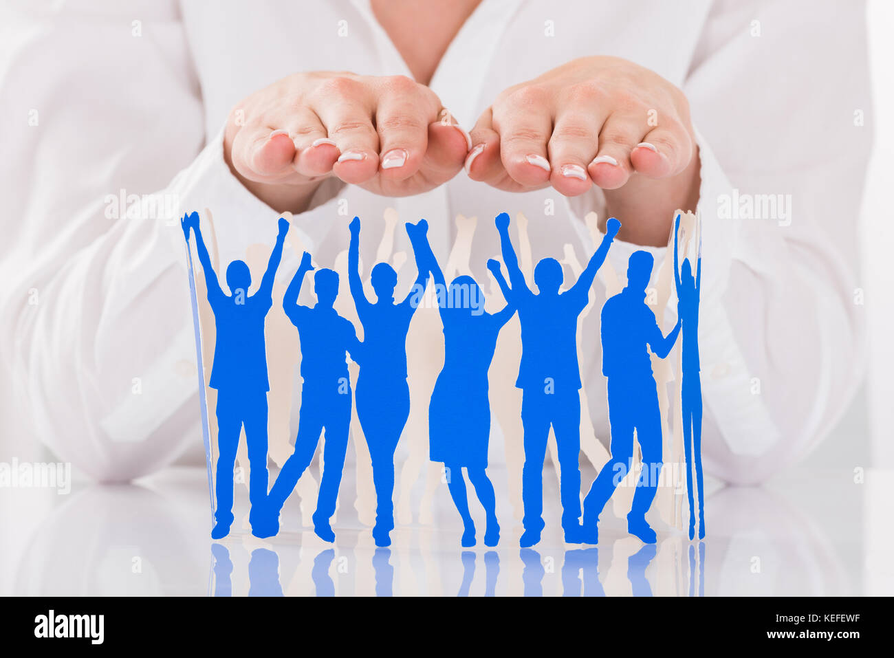 Close-up Of A Person's Hand Protecting Paper Cut Out Of Cheering Human ... Close-up Of A Person's Hand Protecting Paper Cut Out Of Cheering Human ...