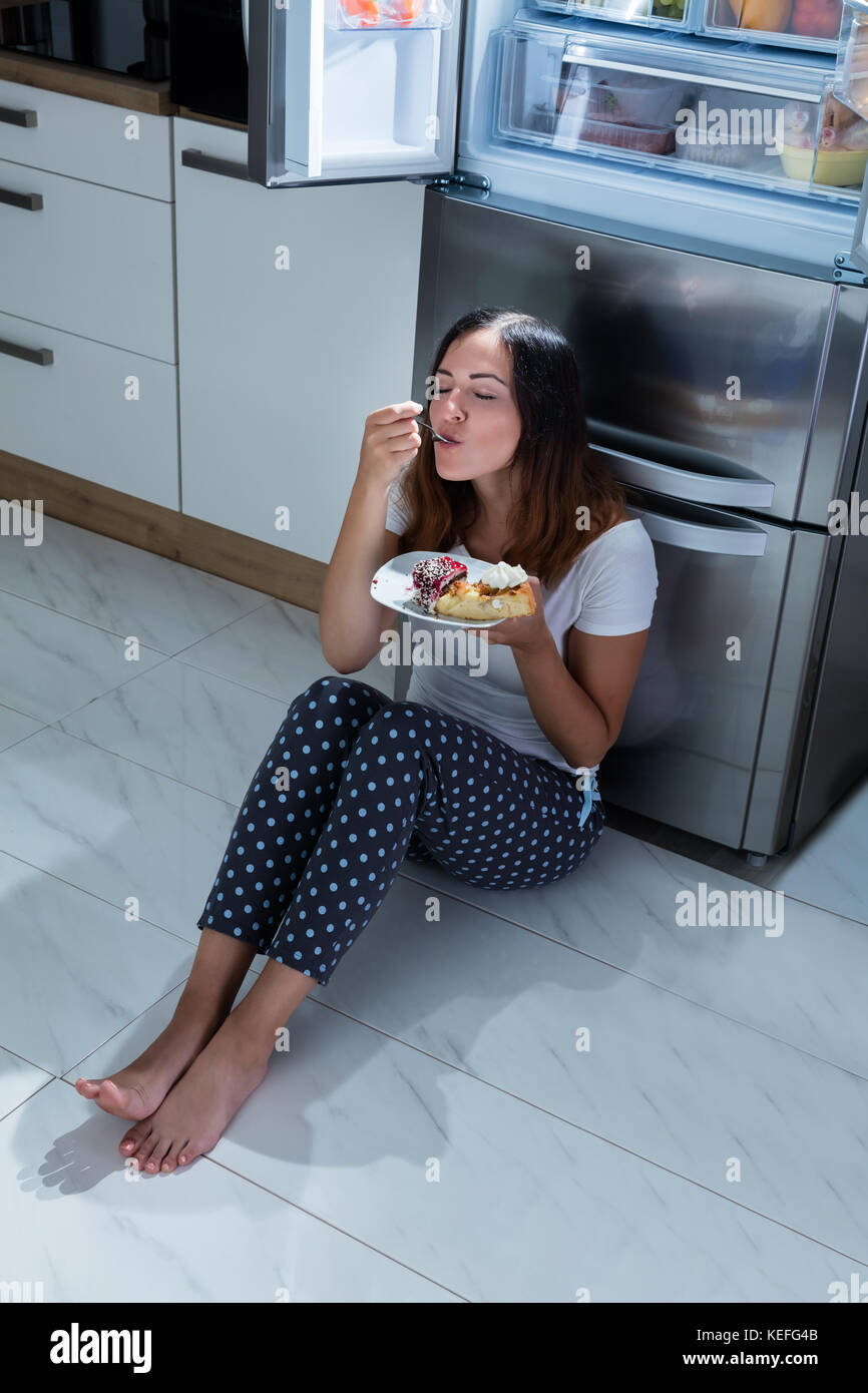Young Woman Enjoy Eating Sweet Food While Sitting On Floor In Kitchen ...
