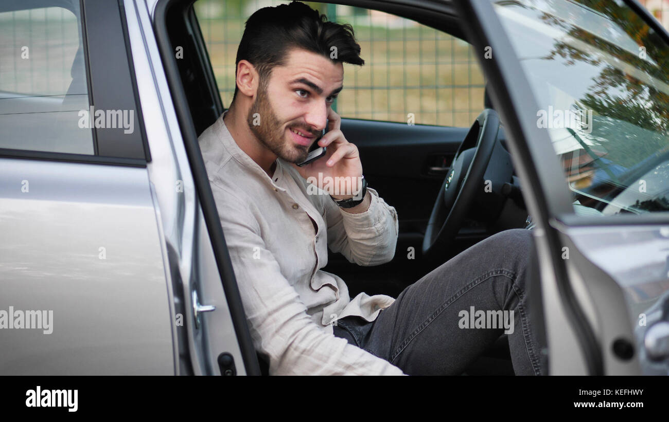 Handsome Young Man talking on mobile phone while sitting in a car with ...