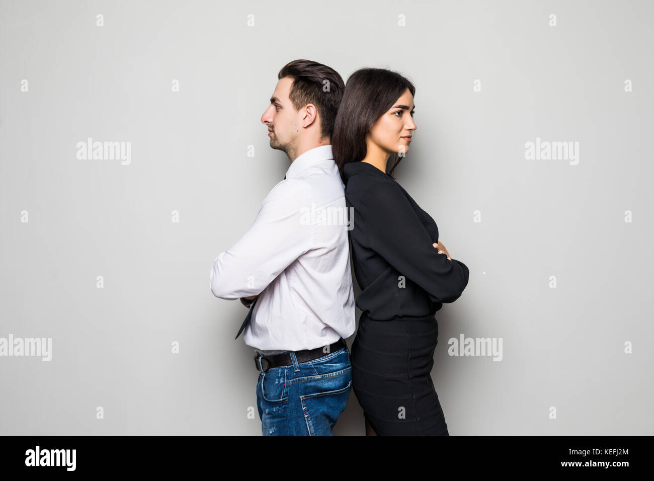 Attractive couple standing back to back both staring thoughtfully into ...