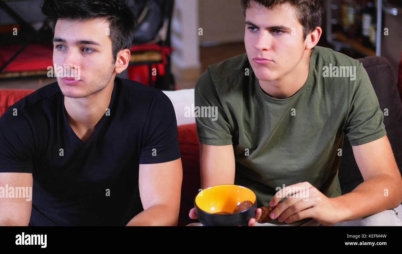 Young male friends chilling on sofa with snacks spending time together ...