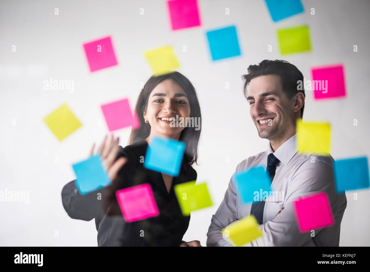 happy creative team writing on stickers at office glass board in modern ...
