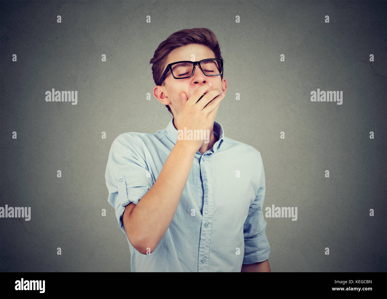 Young man yawning with hand over his mouth Stock Photo - Alamy
