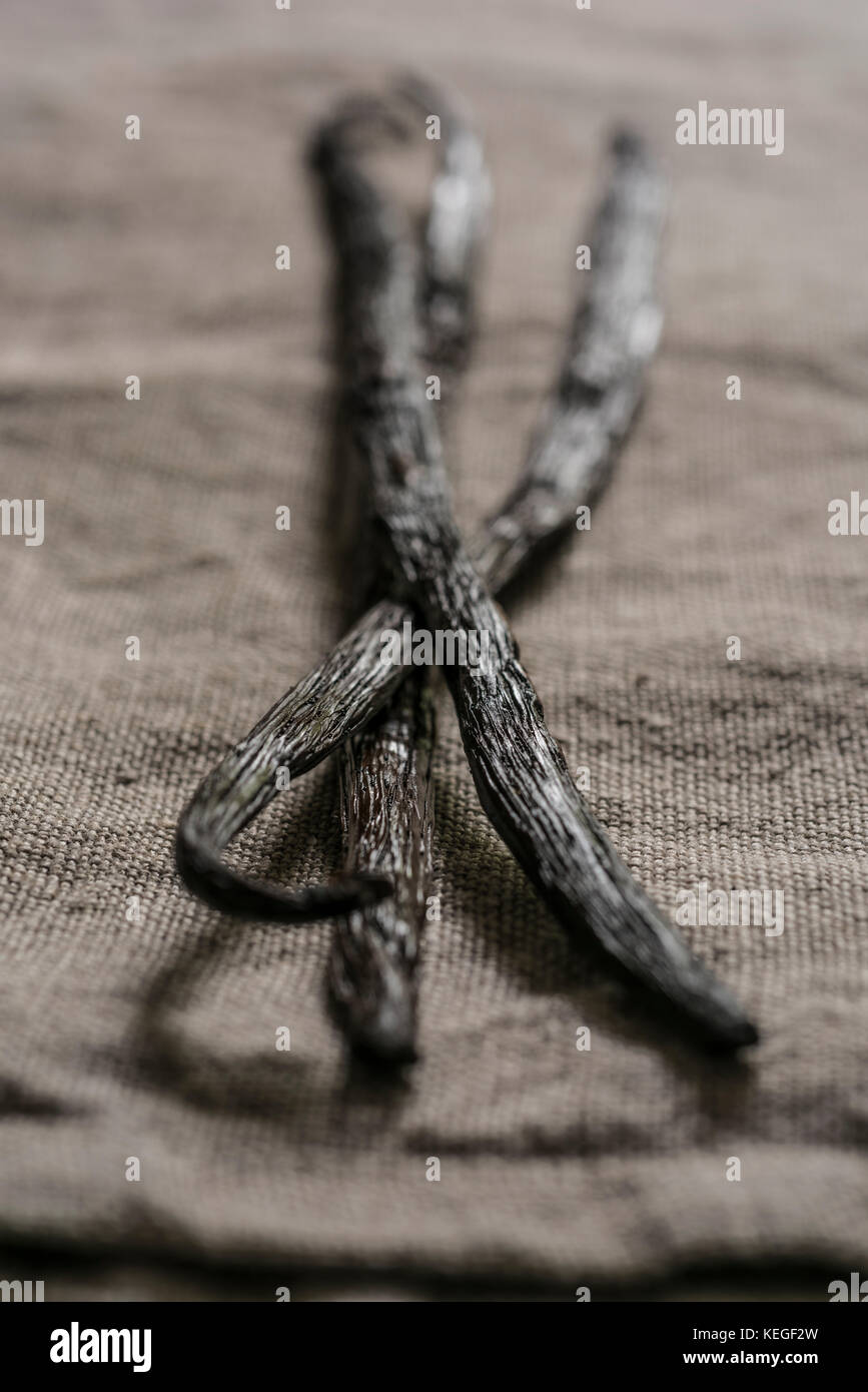 A few slender vanilla pods rest elegantly on a softly textured linen ...