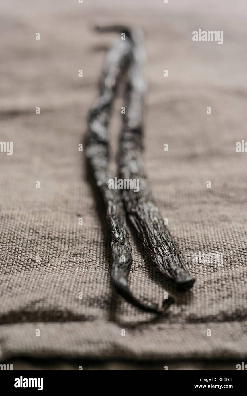 A few slender vanilla pods rest elegantly on a softly textured linen ...