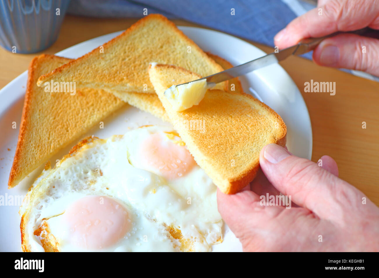Fried eggs and toast on a platter with man buttering toast triangle ...
