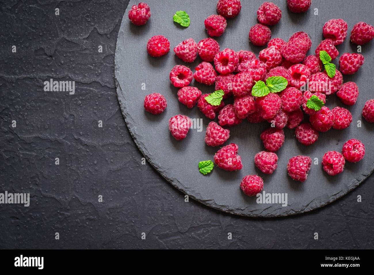 Ripe raspberries on slate dish on black background Stock Photo - Alamy