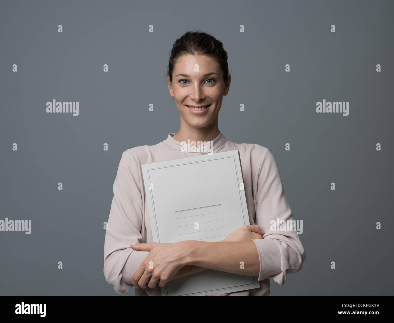 Professional female secretary holding paperwork and smiling at camera ...