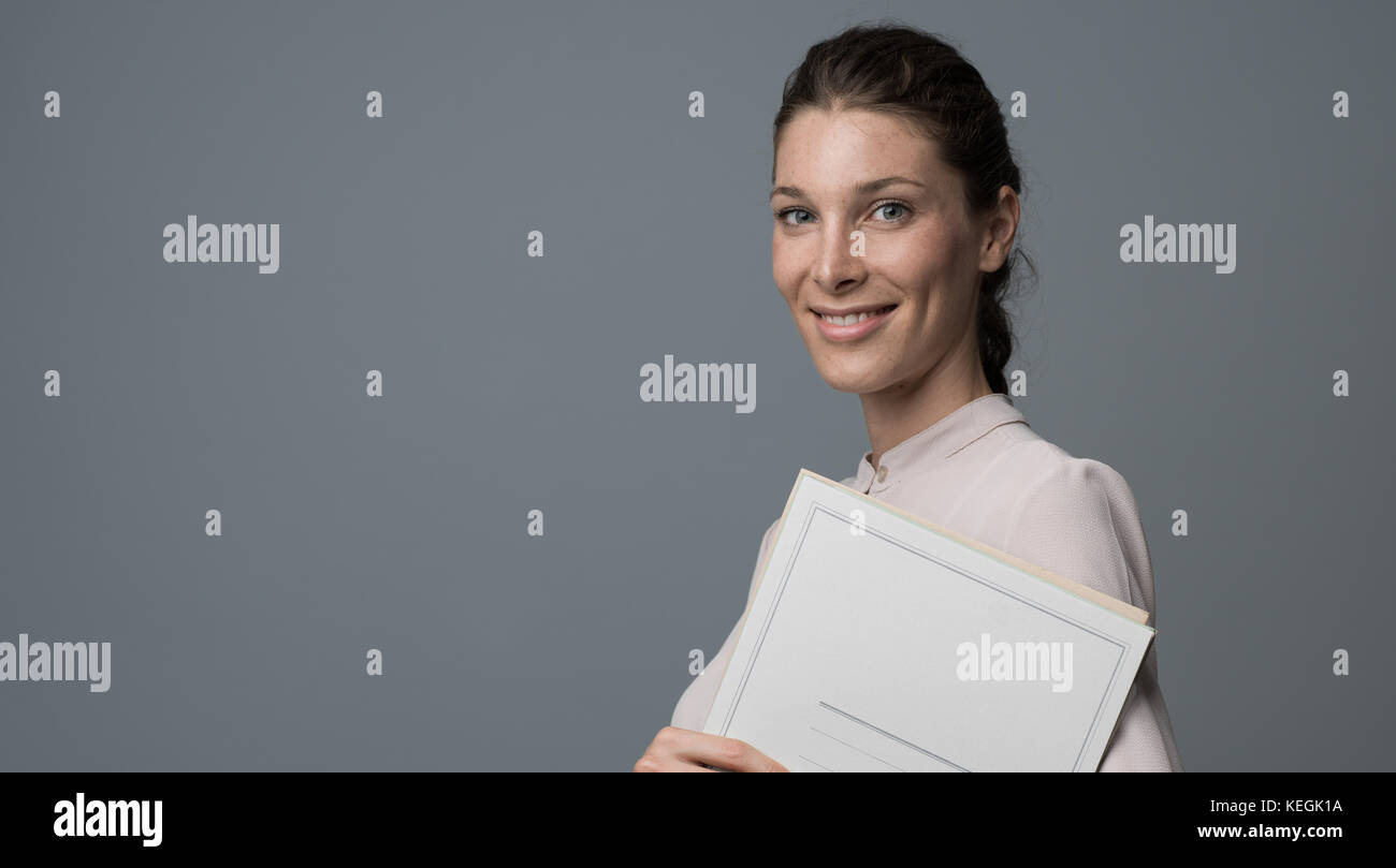 Professional female secretary holding paperwork and smiling at camera ...