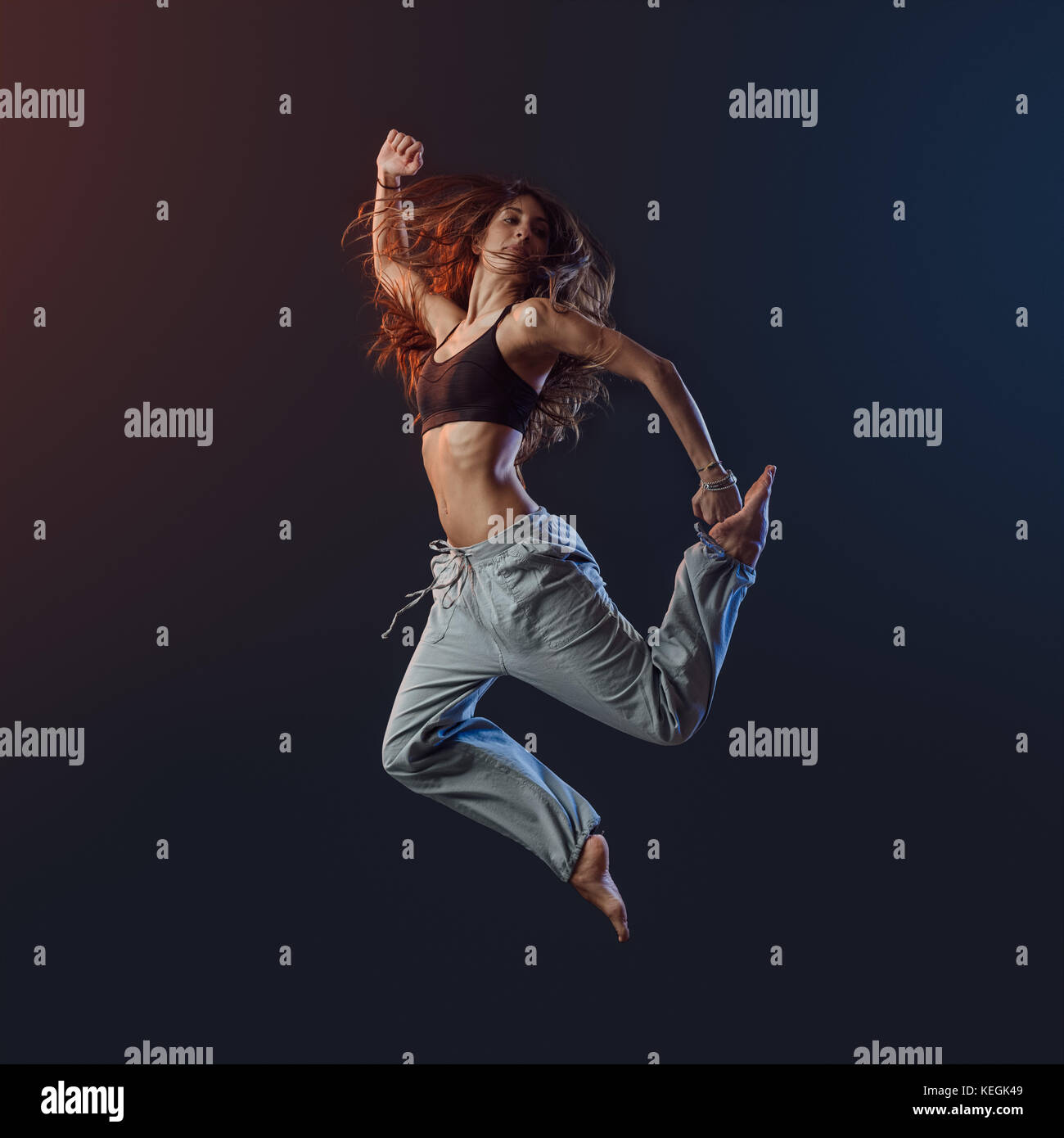 Young athletic slim dancer performing and jumping on dark background ...