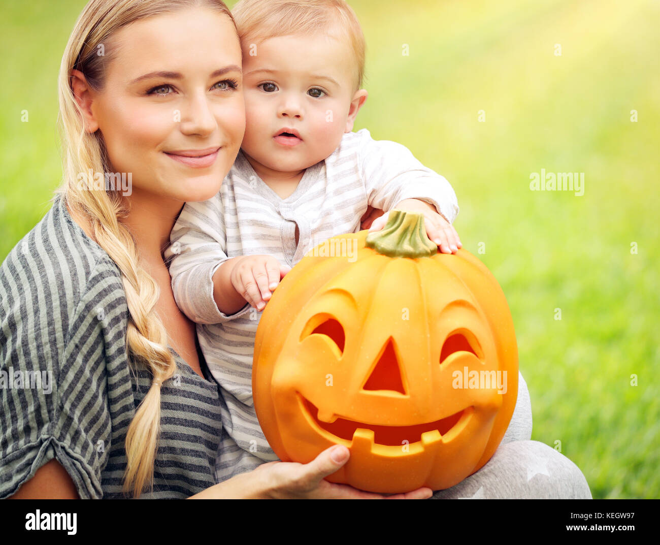 Portrait of a nice mother with her cute little son holding in hands funny carved pumpkin ...