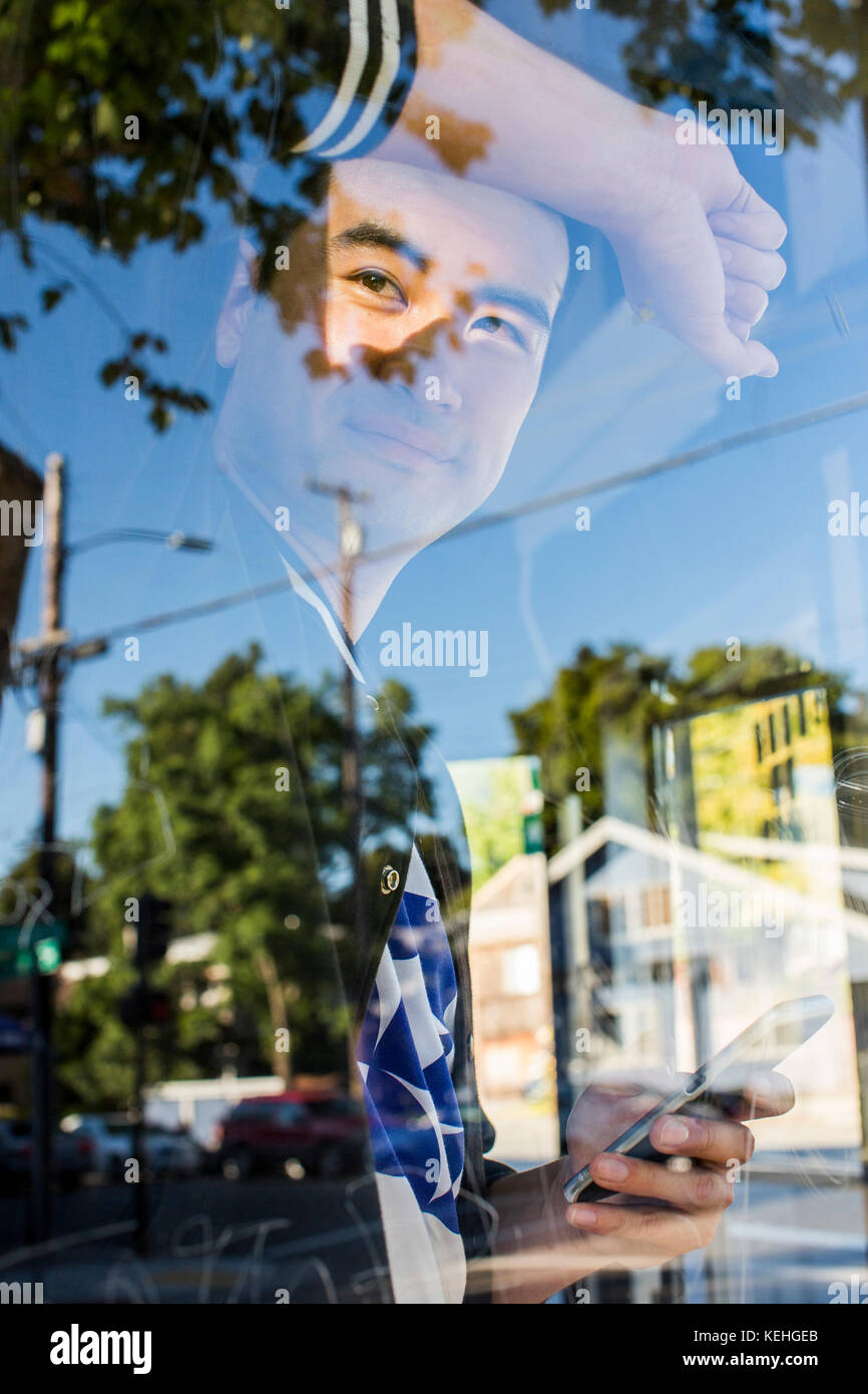 Smiling Chinese man leaning on window holding cell phone Stock Photo ...