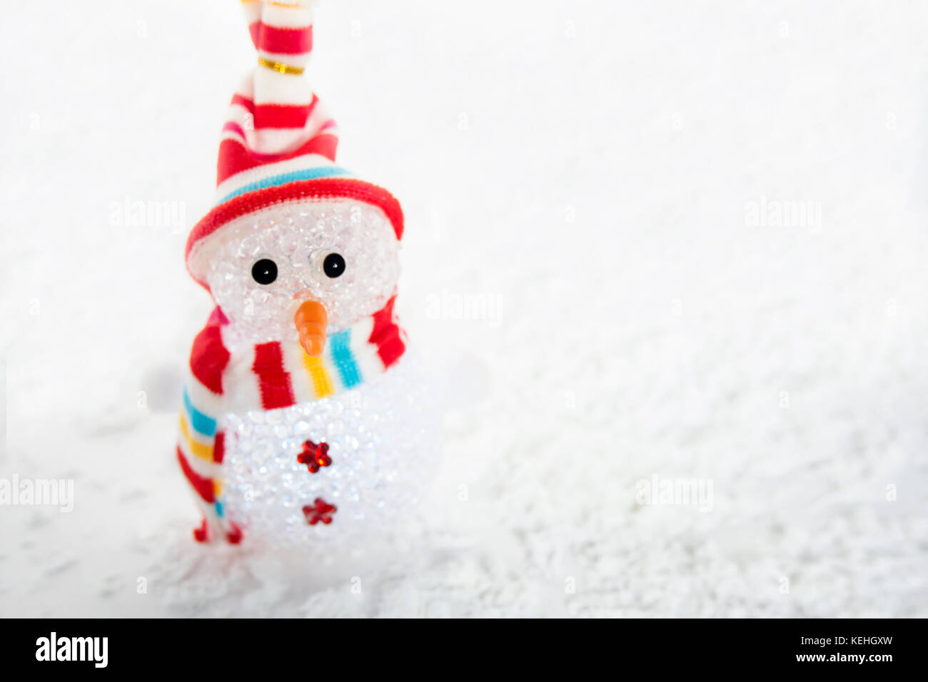 Snowman in striped colorful cap and scarf on the snow background ...
