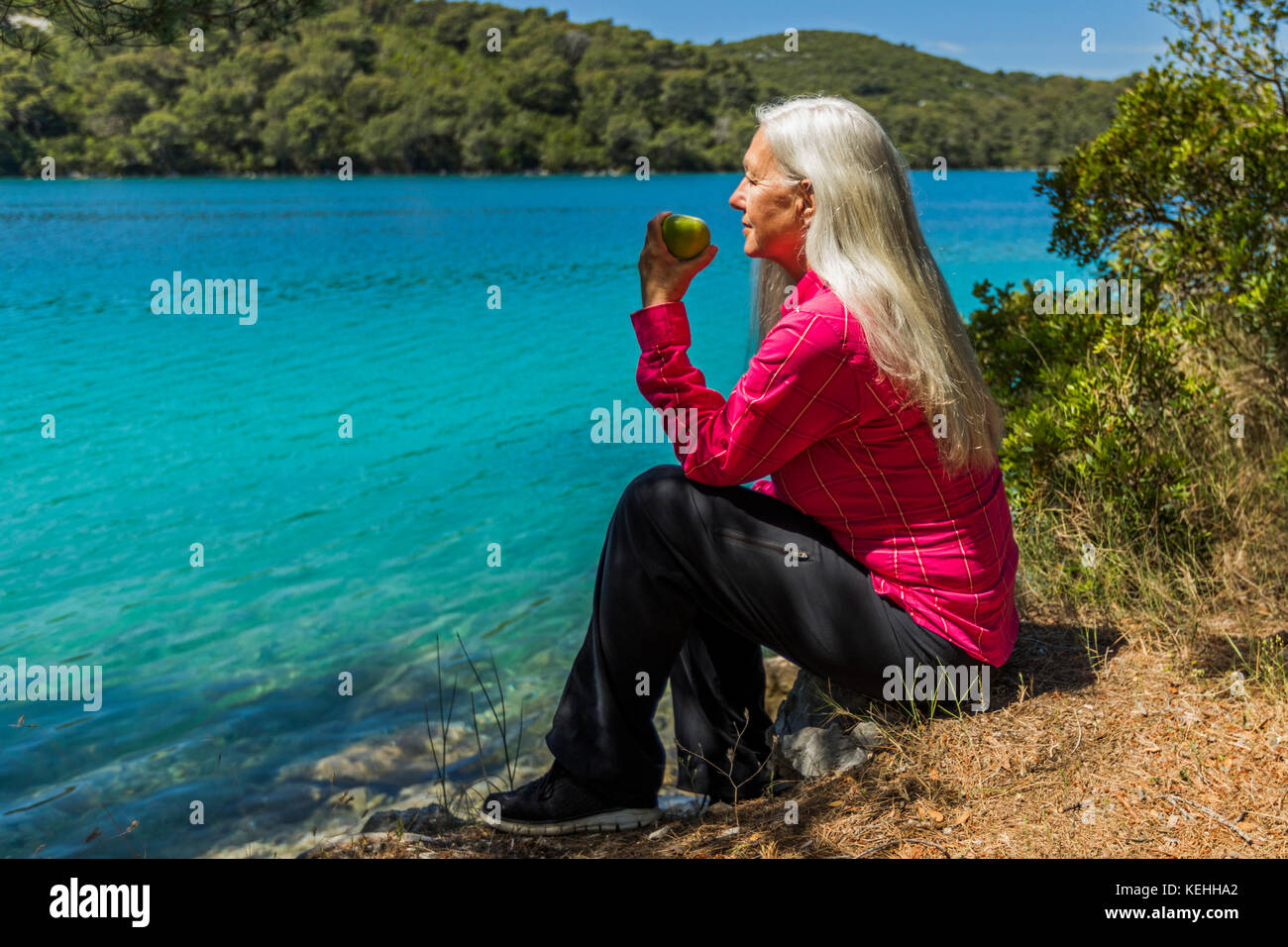 Caucasian woman sitting at lake eating apple Stock Photo - Alamy