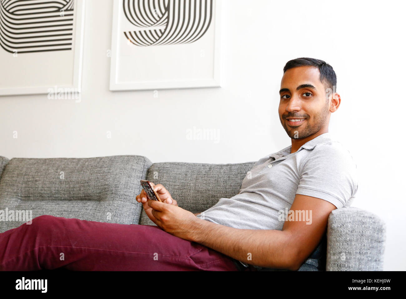 Mixed race man sitting on sofa texting on cell phone Stock Photo - Alamy