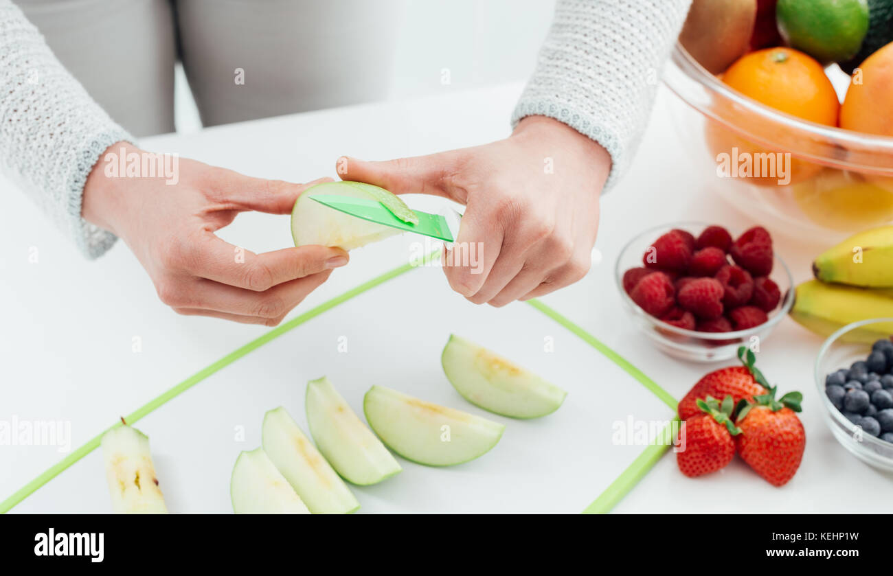Woman preparing fruit in her kitchen, she is slicing and peeling apples ...