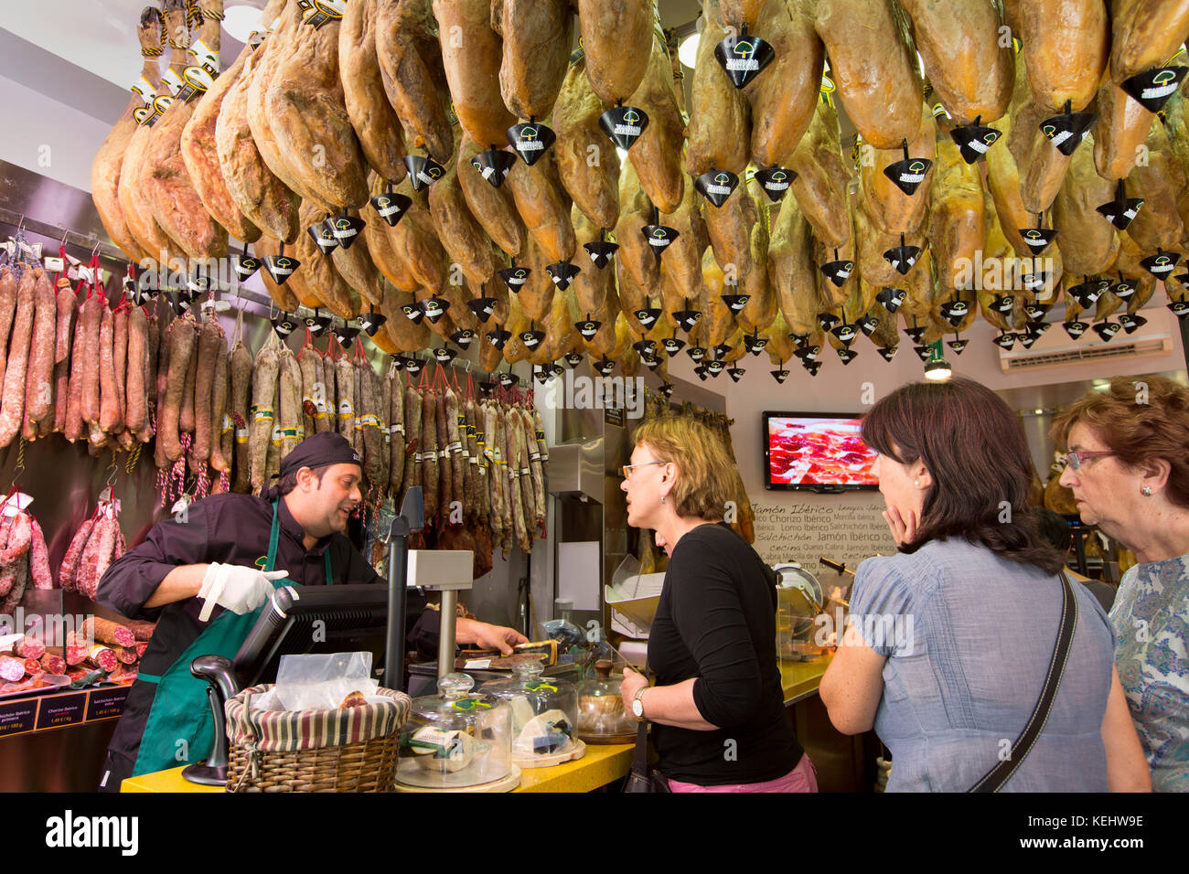 Shoppers in butcher's shop to buy Iberico Jamon Ham and other meats in ...