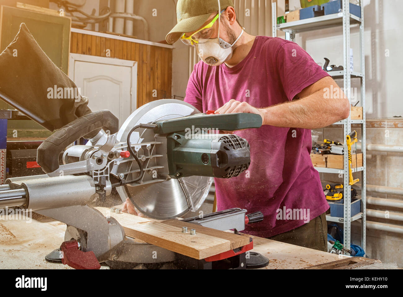 A man carpenter with work clothes and a cap cuts a wooden board on a ...