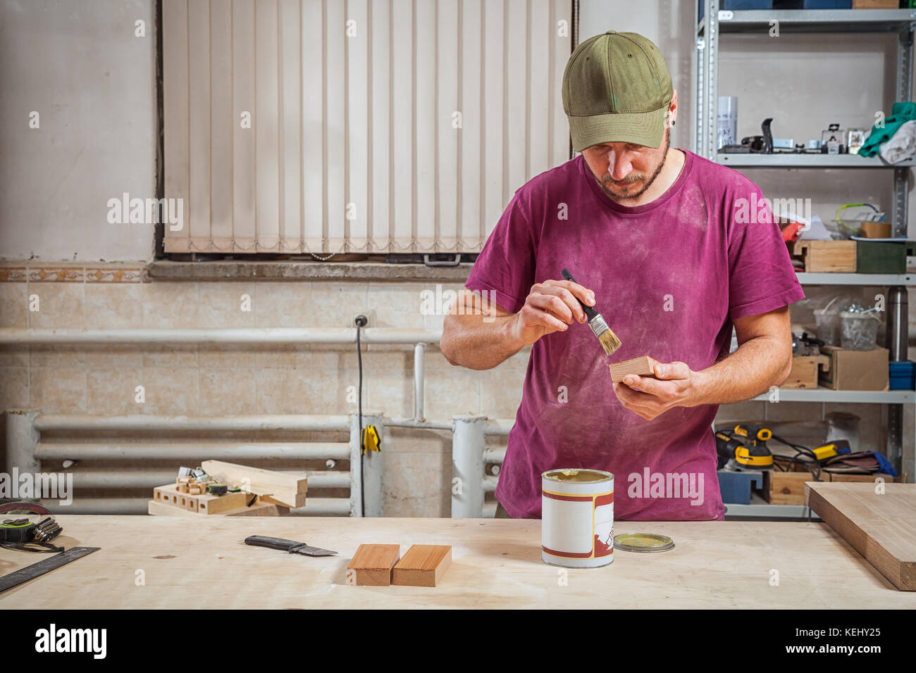 Close-up The man carpenter in working clothes paints a wooden block ...