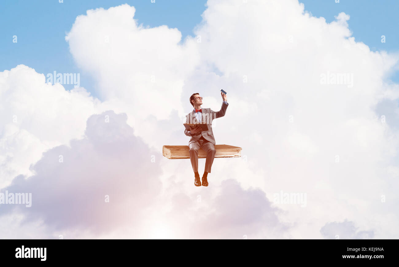 Young businessman or student floating in blue sky and studying the ...