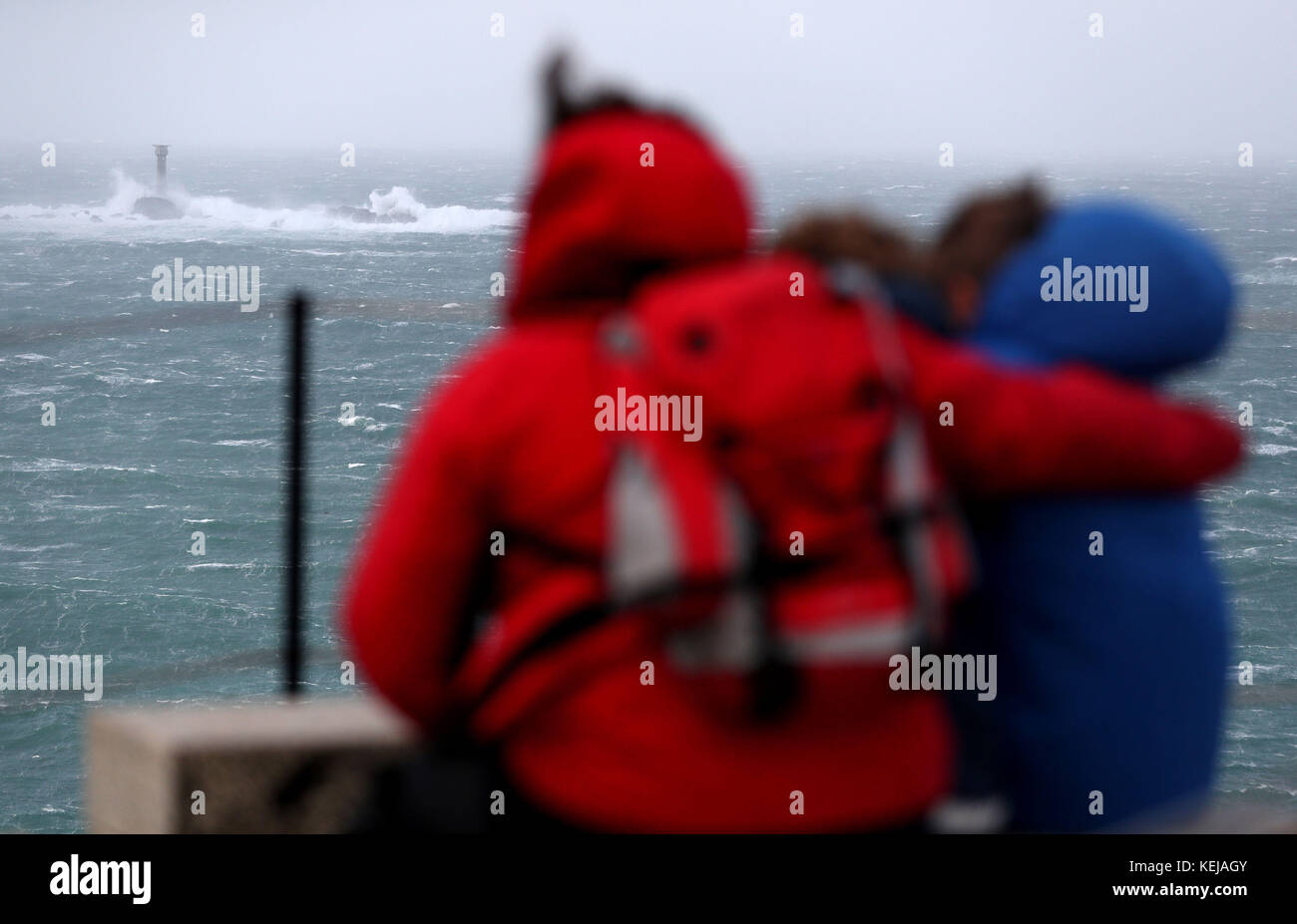 People watch the waves crash around Longships lighthouse on the cliffs ...