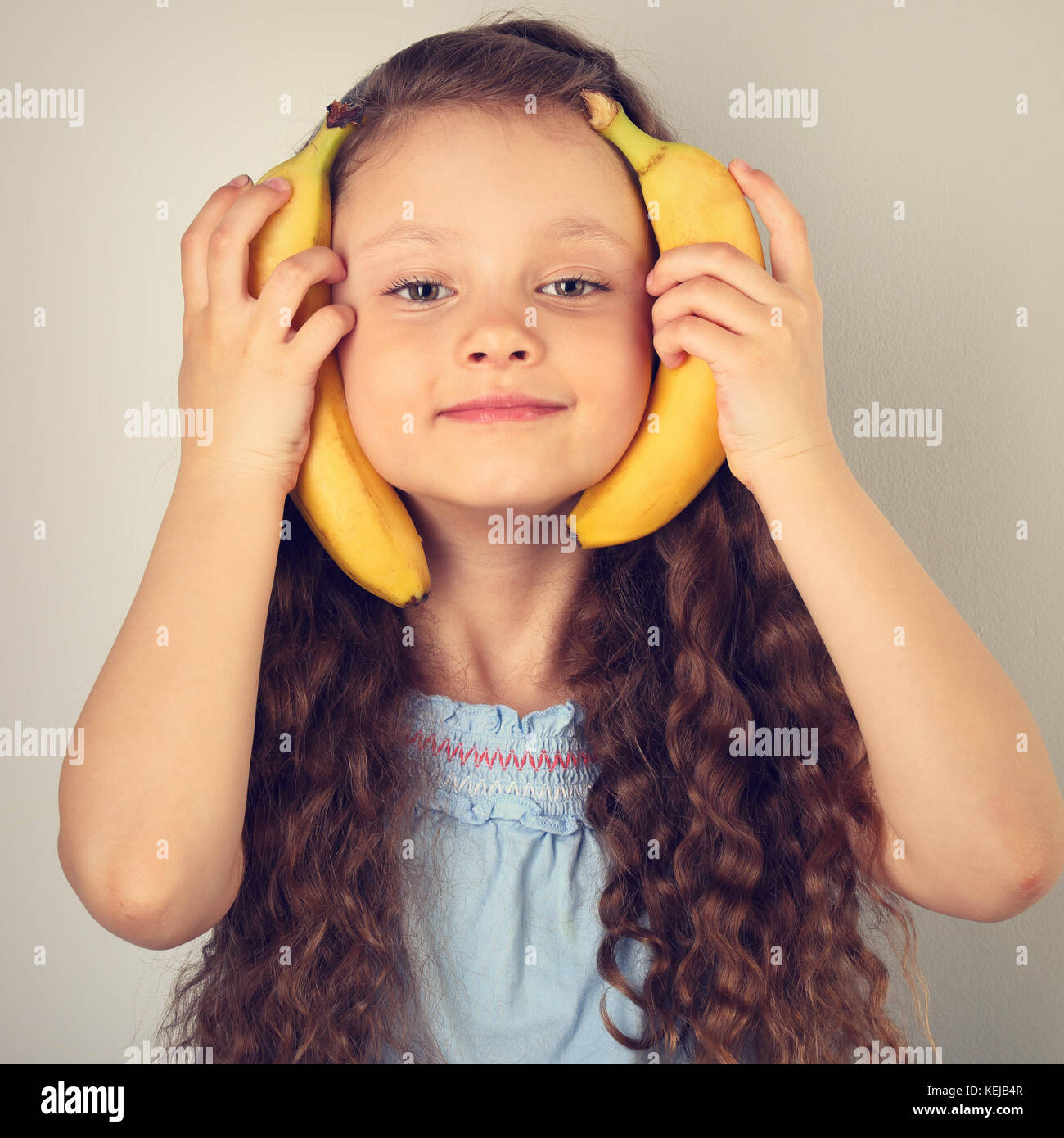 Playful happy fun long hair kid girl holding yellow bright bananas near ...