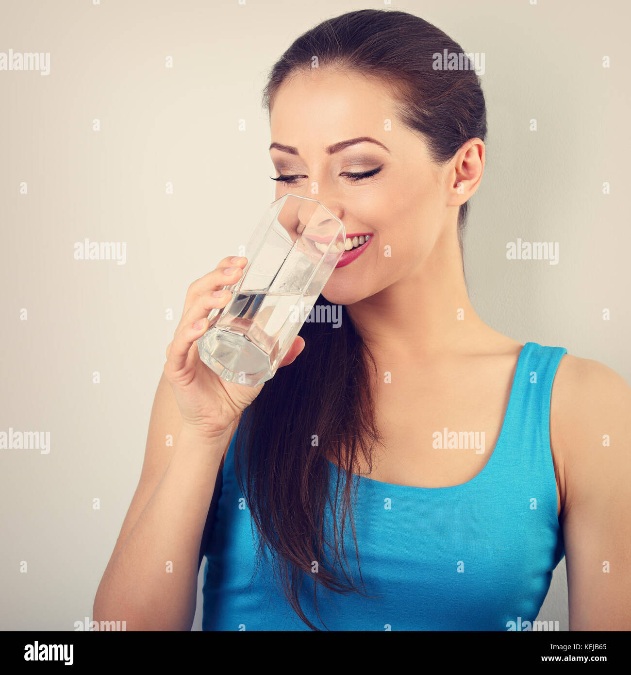 Young beautiful woman drinking fresh pure water from glass on blue ...