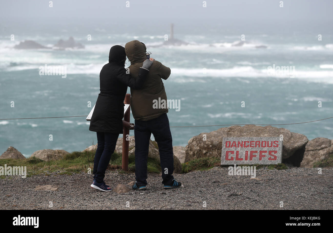 People look out from the cliff top as waves crash around the Longships ...
