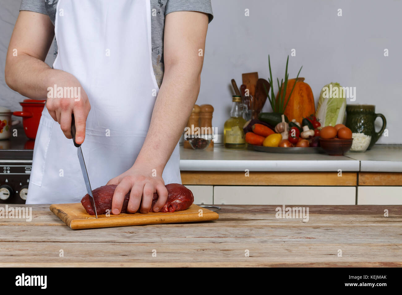 Man in the kitchen cutting a piece of meat. preparation Stock Photo - Alamy