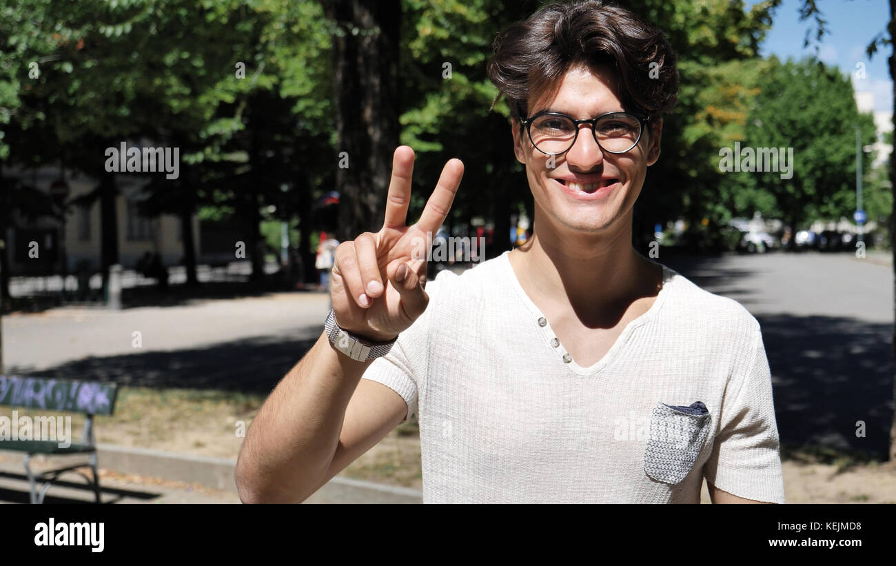 Handsome young man at city park doing victory sign with fingers ...