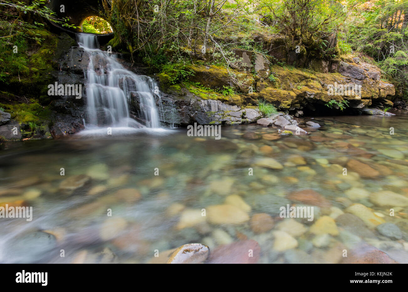 Waterfall from drainage pipe into river with colorful river rocks Stock ...