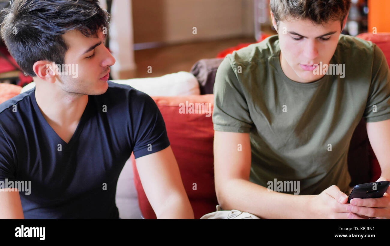 Two young male friends talking and chatting while sitting on sofa at ...