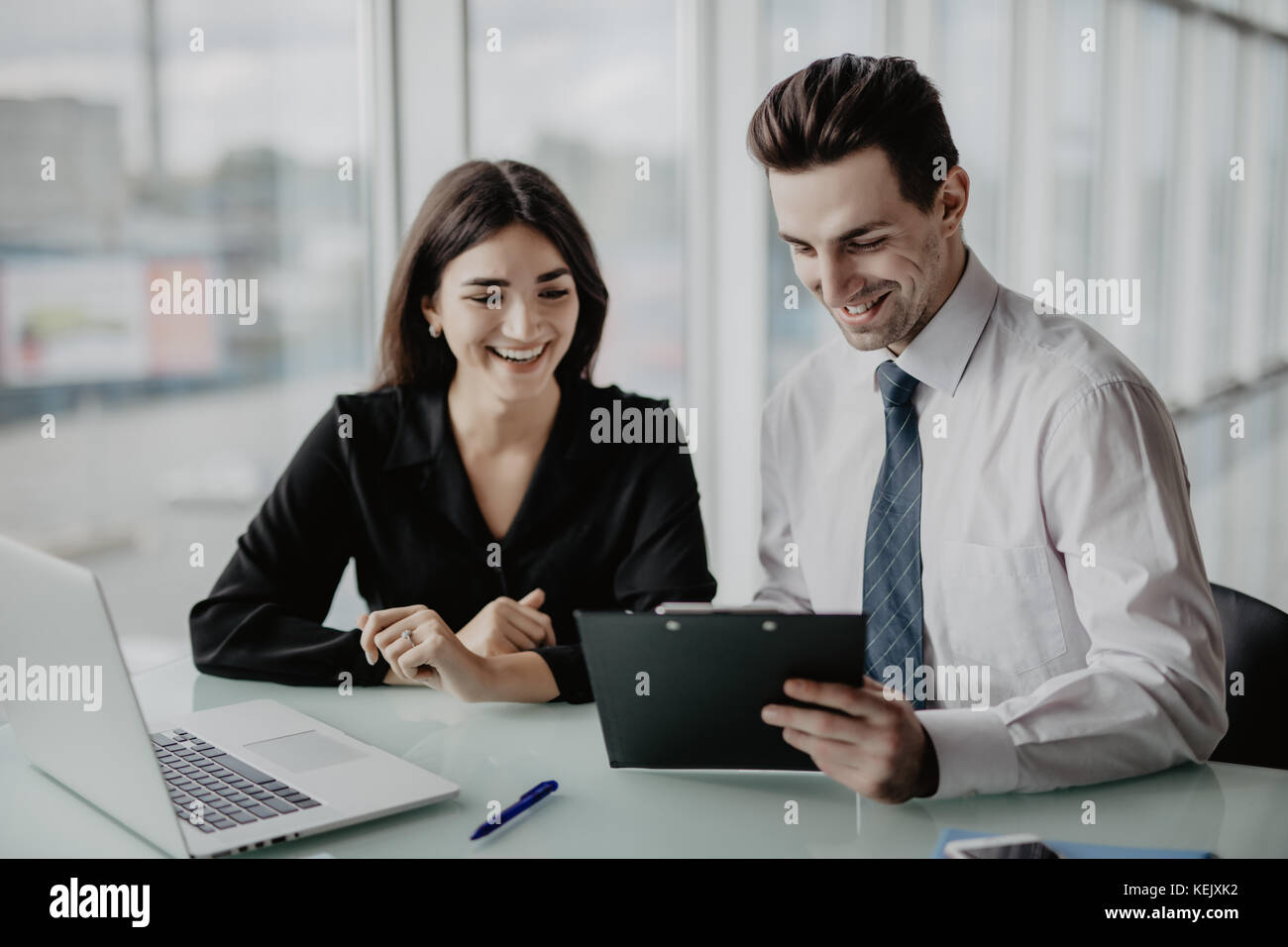 Two entrepreneurs sitting together working in an office desk comparing ...