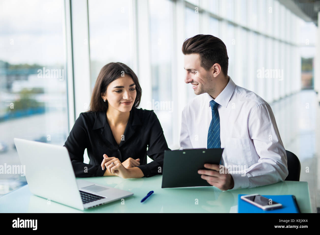 Client signing a document in an office with a businesswoman looking the ...