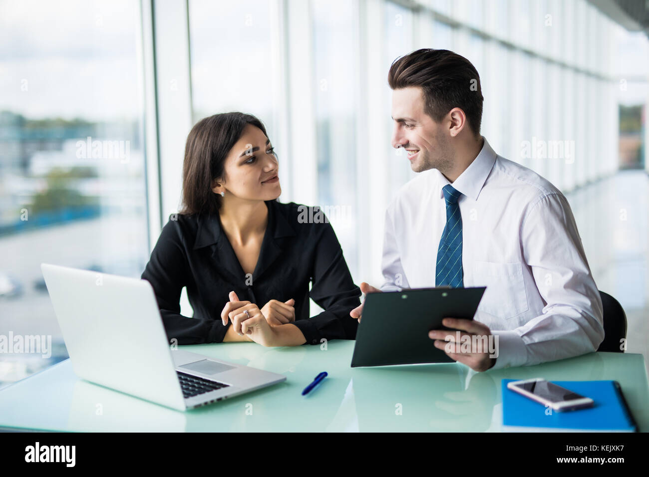 Client signing a document in an office with a businesswoman looking the ...