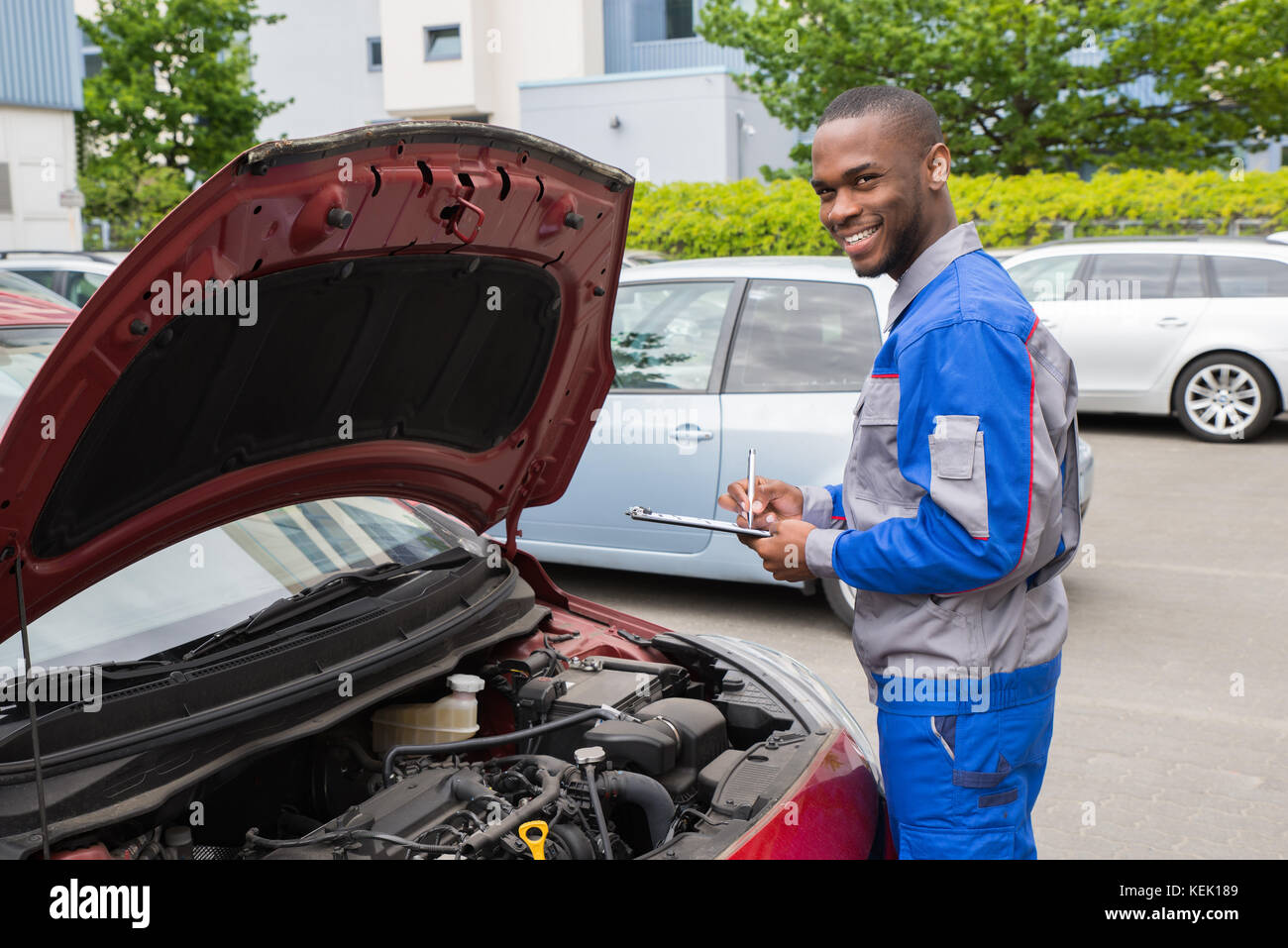 Young African Mechanic Writing On Clipboard In Front Of Open Car Engine ...