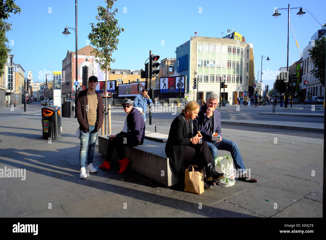 People young and old sitting & eating near a bus stop on old street ...
